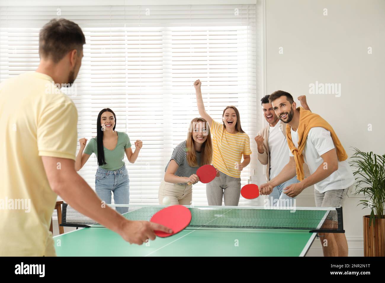 Happy friends playing ping pong together indoors Stock Photo - Alamy