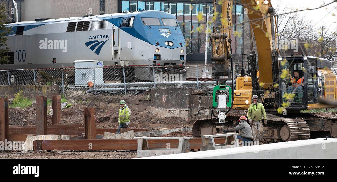 Crews work on a steel beam frame as an Amtrak train passes by the flood ...