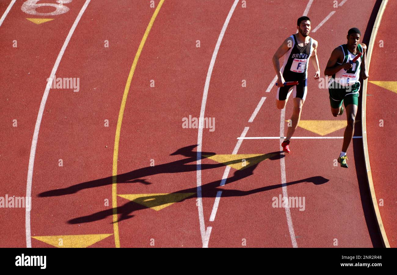 Runners cast shadows on the track during a college men's 4 x 400-meter ...