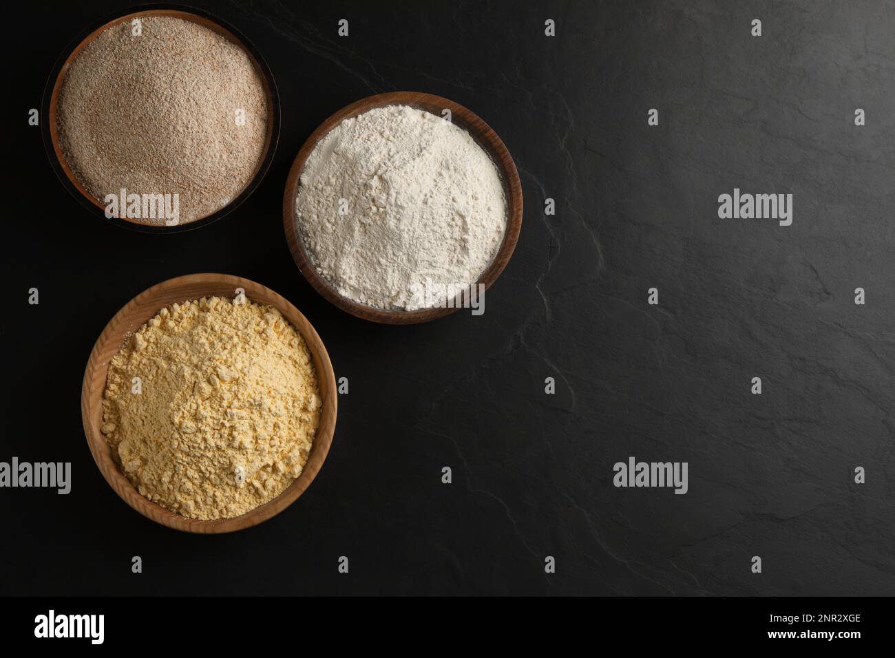 Different types of flours on black table, flat lay. Space for text ...
