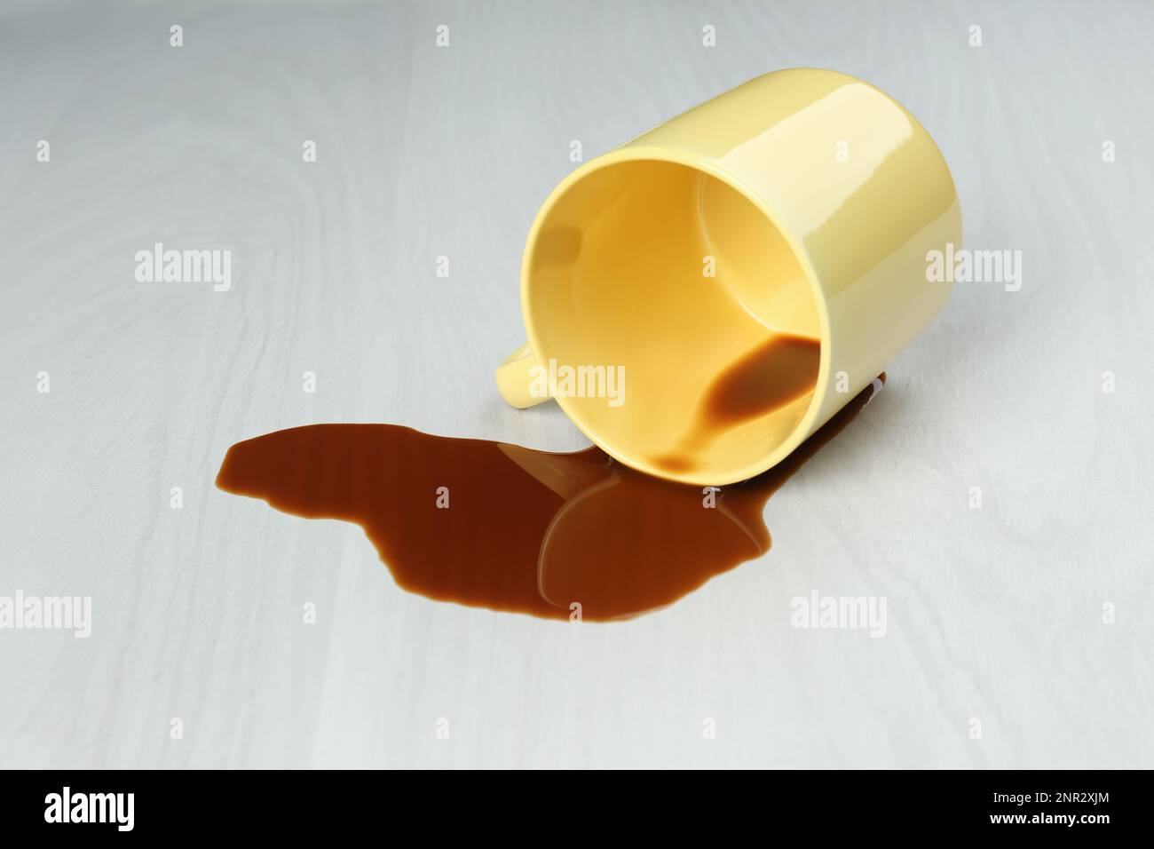 Overturned cup and spilled coffee on white wooden table Stock Photo - Alamy