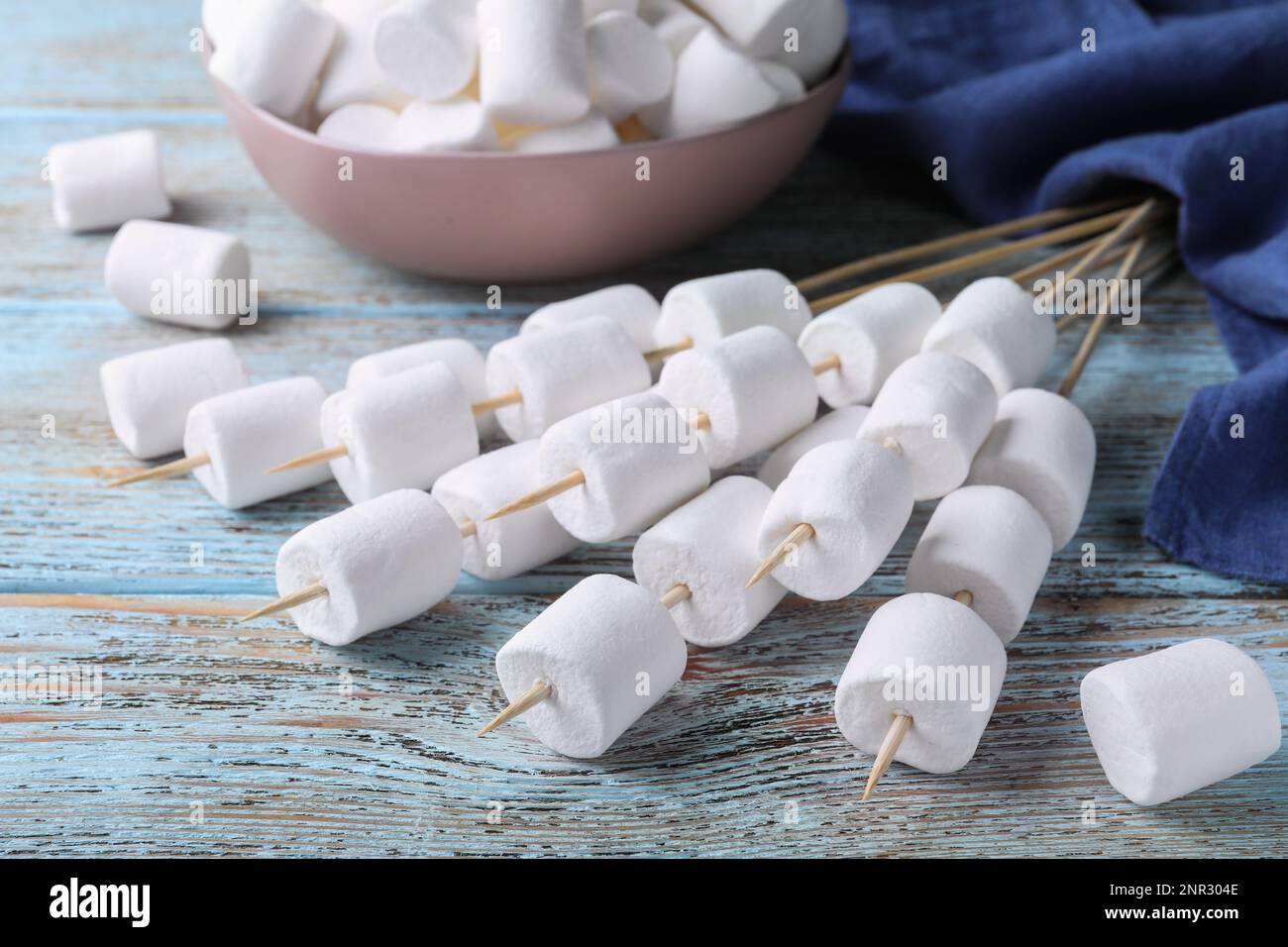 Sticks with delicious puffy marshmallows on light blue wooden table ...