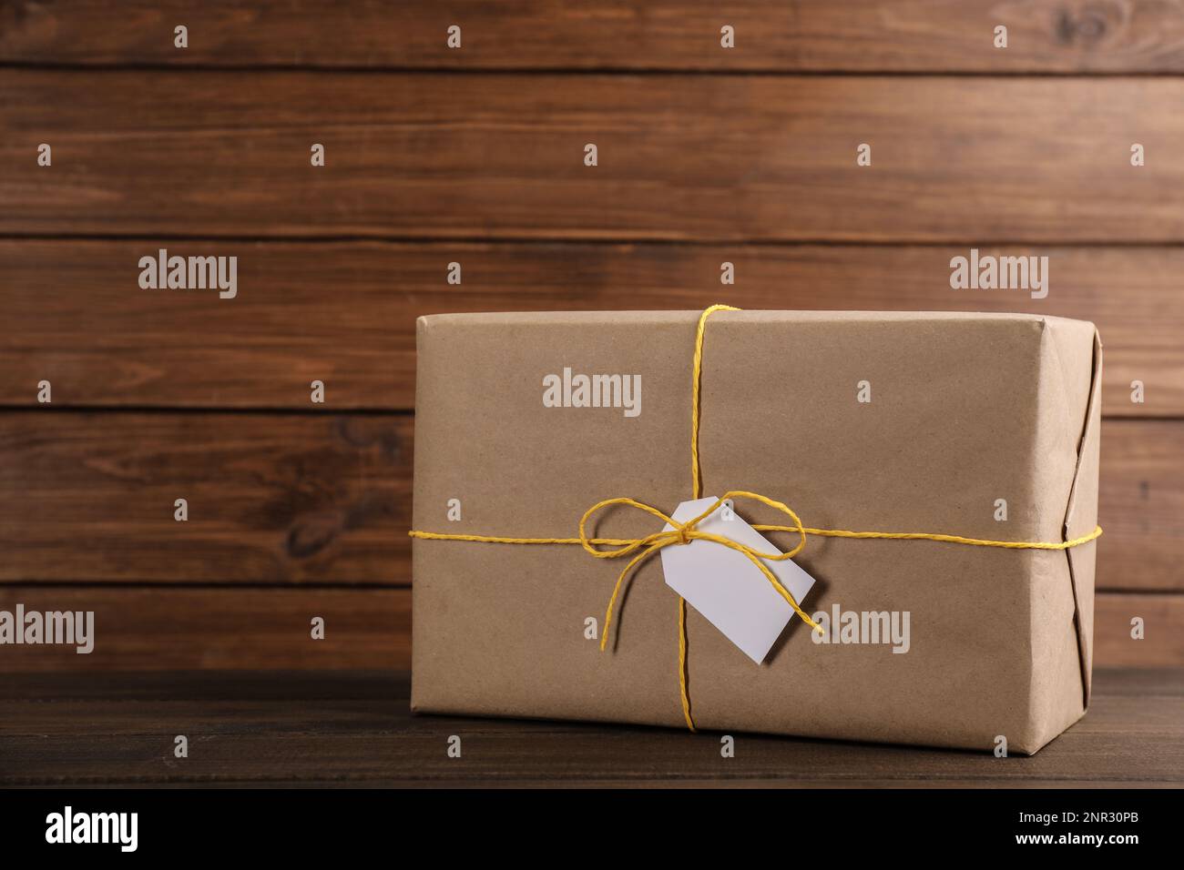 Parcel wrapped in kraft paper with tag on wooden table, space for text ...