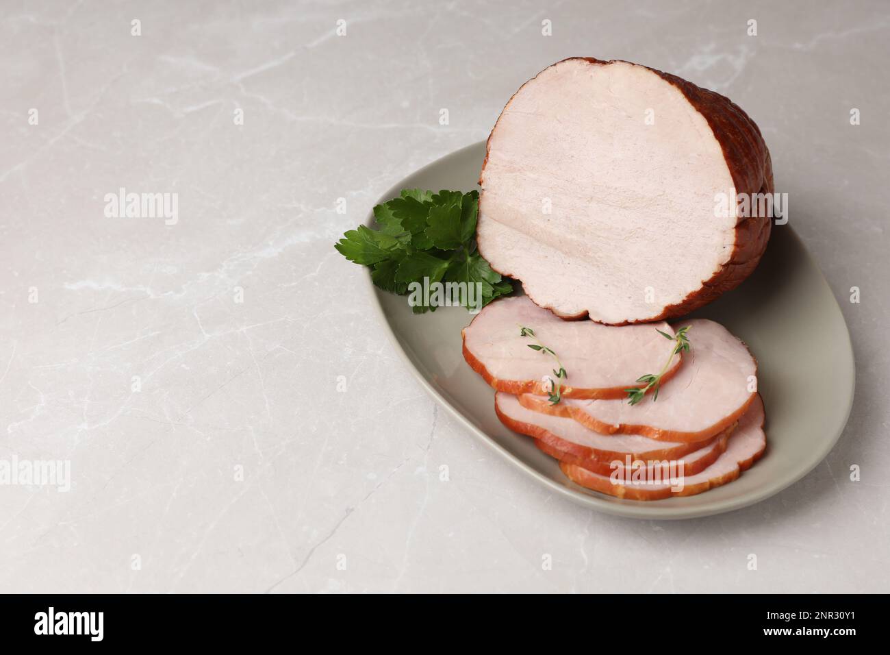 Delicious cut ham with aromatic herbs on light grey table, space for ...