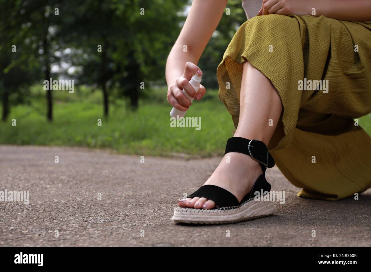 Woman applying insect repellent onto leg in park, closeup. Tick bites ...