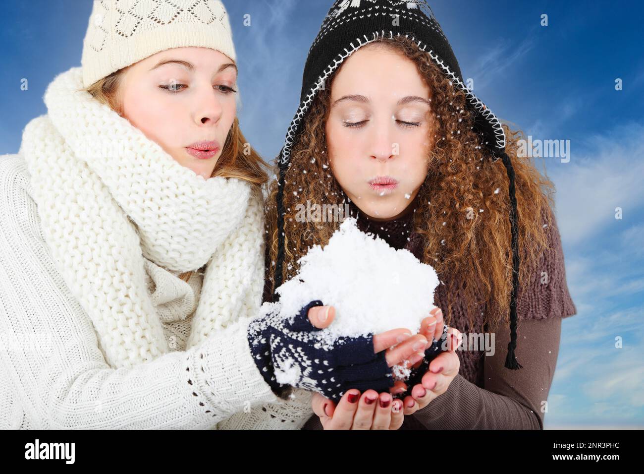 Two young woman blow the snow off their hand Stock Photo - Alamy