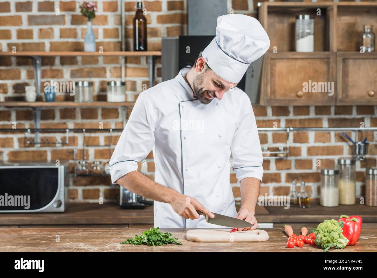 happy young male chef cutting red chili with knife kitchen counter ...