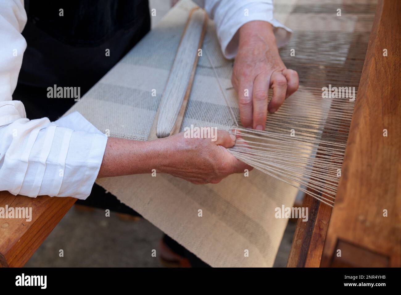 Close up on the hands of a man weaving a canvas from flax fibers with ...