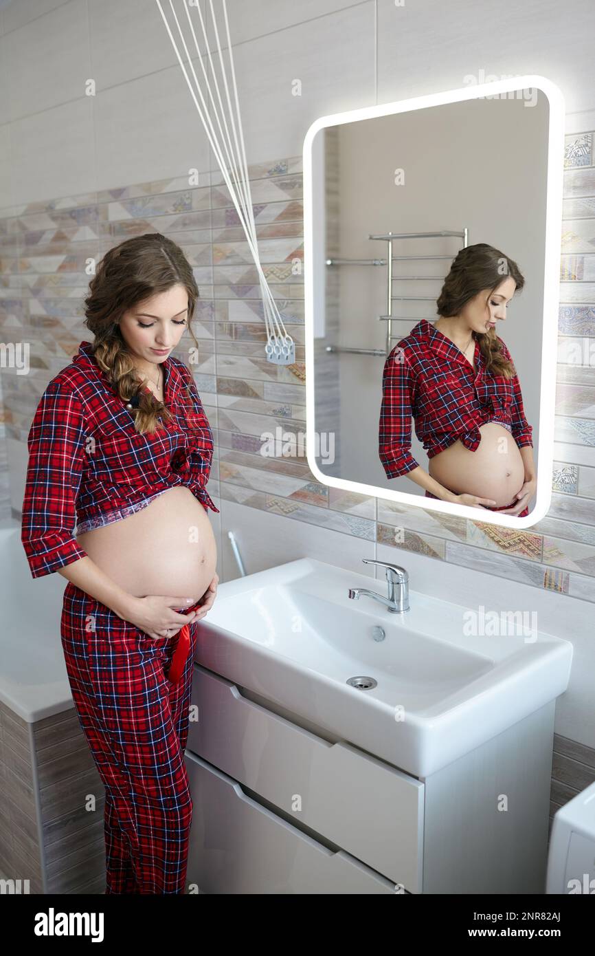 A pregnant woman in the bathroom looks at her pregnant belly. Female ...