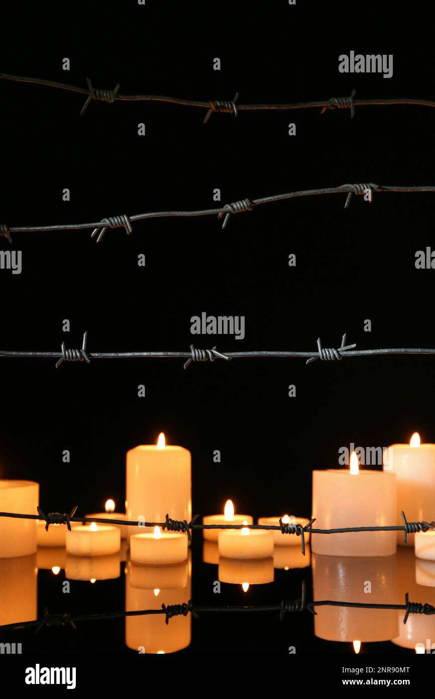 Barbed wire and burning candles on glass table against dark background ...