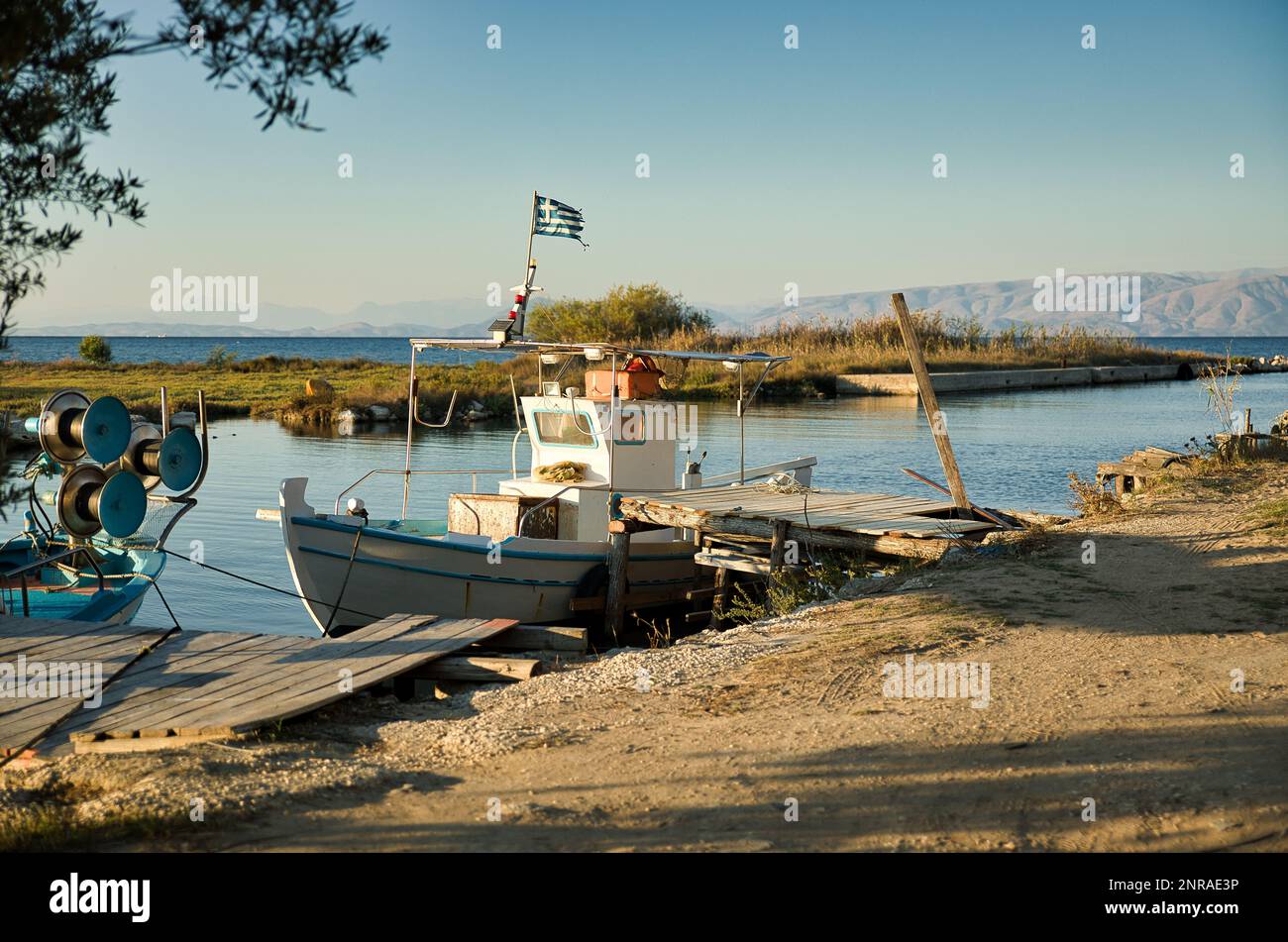 A wooden boat at anchor in a sunlit setting on a jetty and sandy path ...