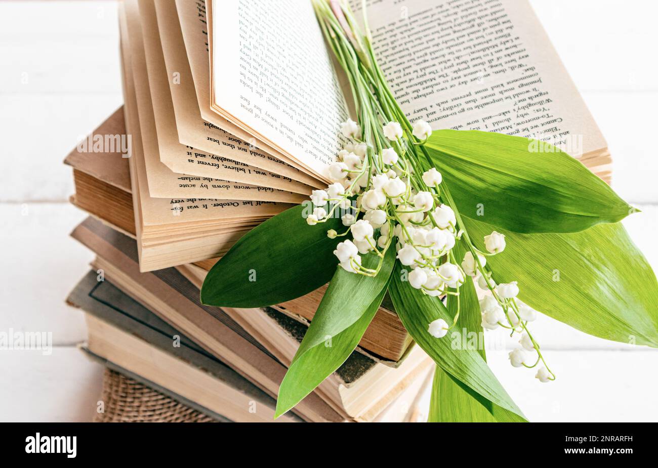 a stack of old books and a bouquet of spring lilies of the valley on an ...
