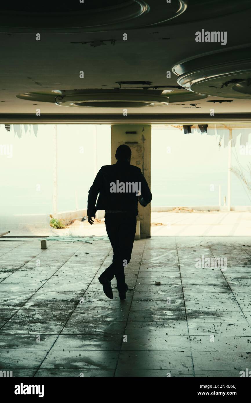 Rear view of mysterious male figure running inside a derlict building ...