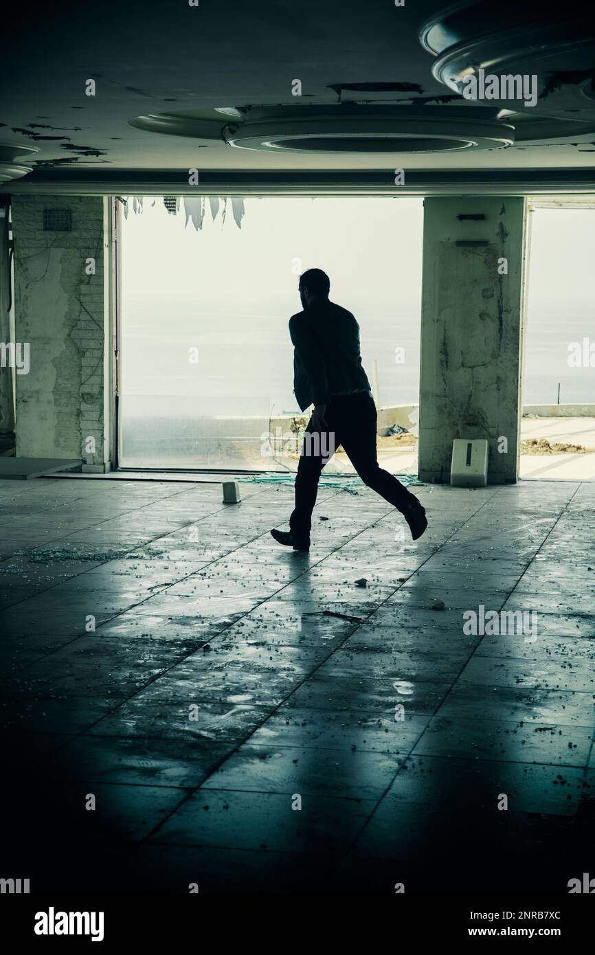Rear view of mysterious male figure running inside a derlict building ...