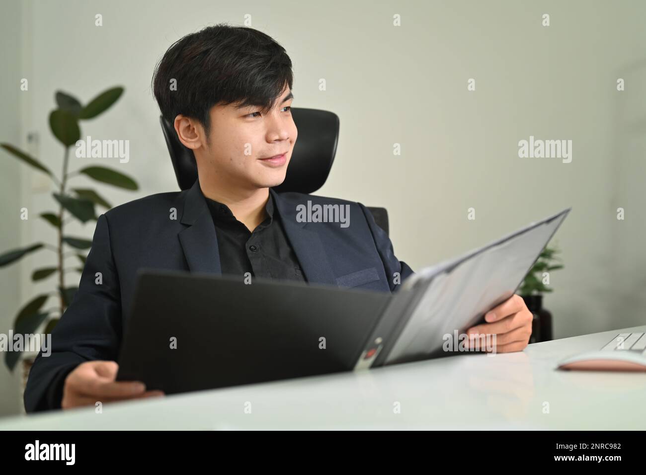 Portrait of asian businessman sitting at his workplace holding binder ...