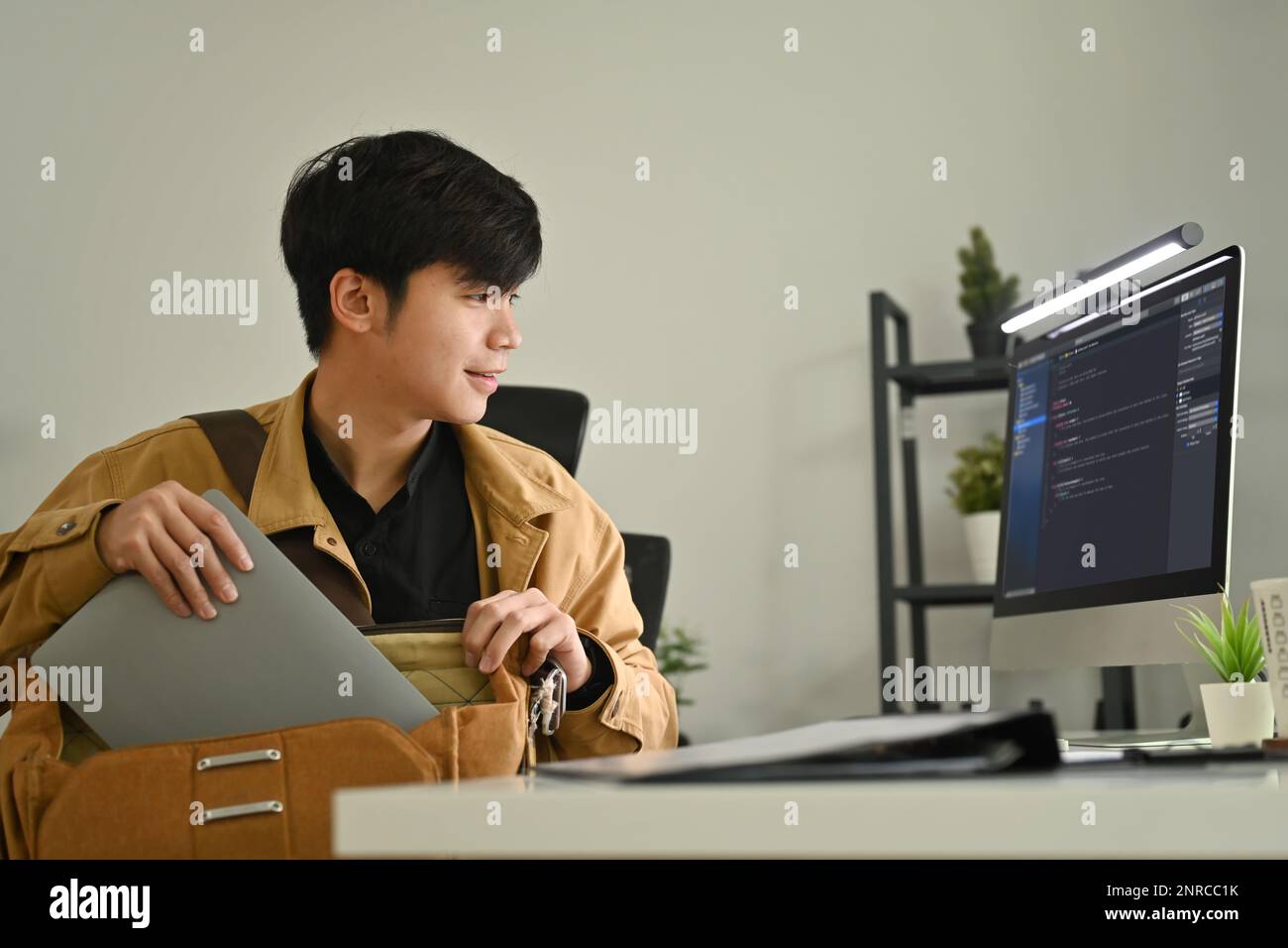 Asian male programmer sitting front of computers with coded data on screen putting his stuff ...