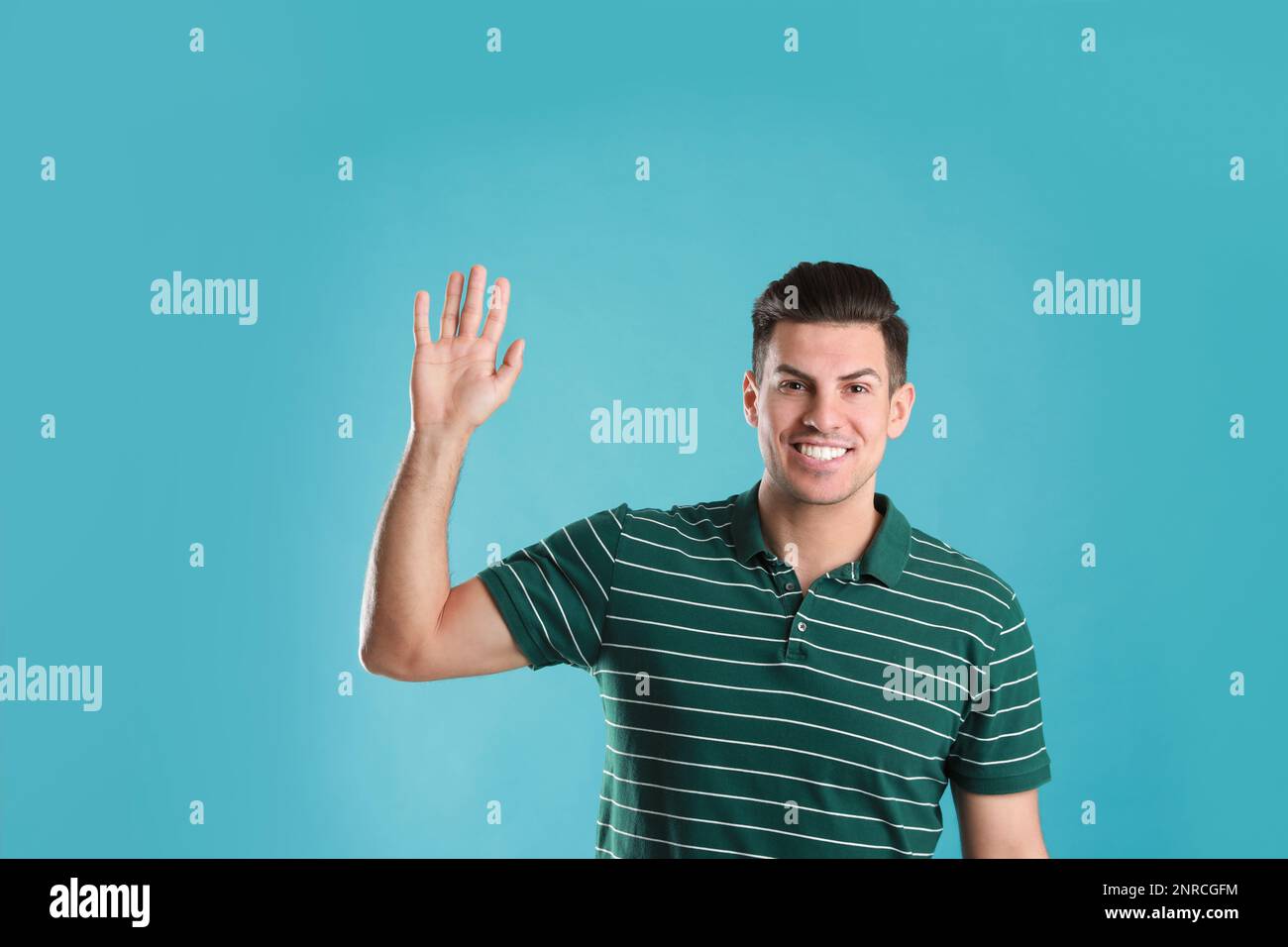 Cheerful man waving to say hello on turquoise background Stock Photo ...