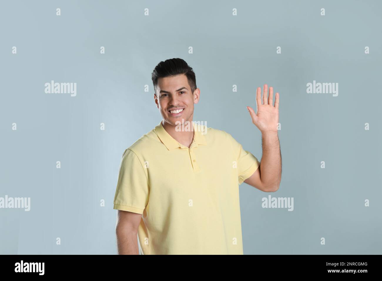 Cheerful man waving to say hello on grey background Stock Photo - Alamy