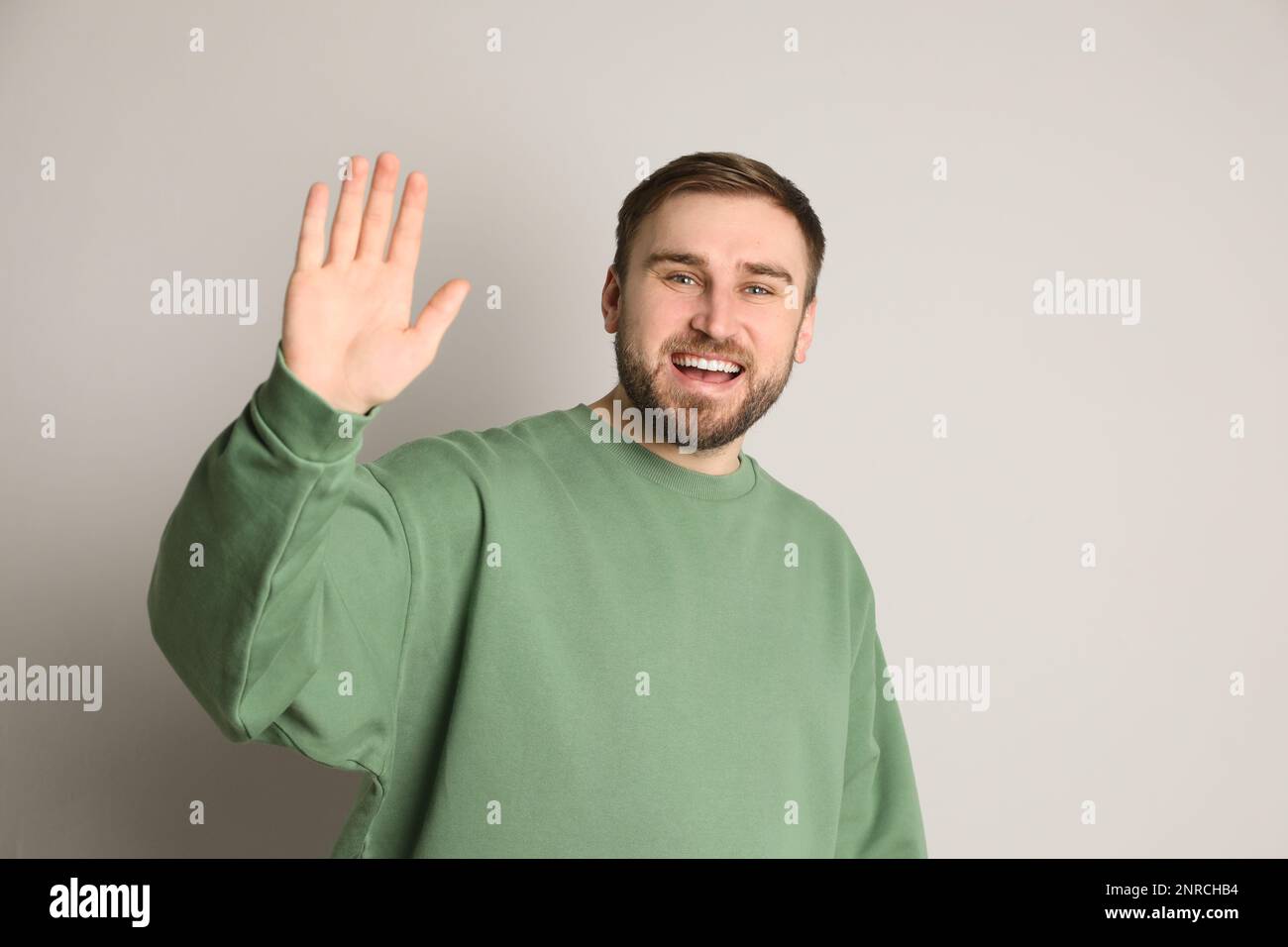 Happy young man waving to say hello on light grey background Stock ...