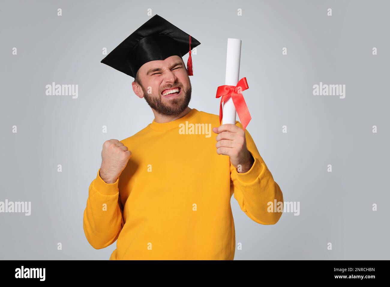Emotional student with graduation hat and diploma on light grey ...