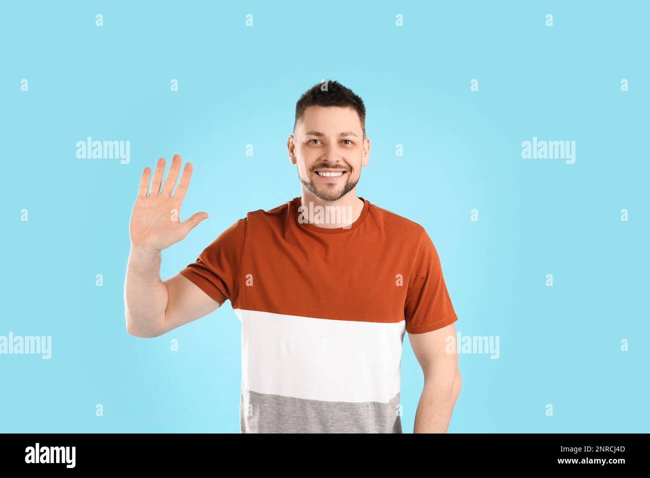 Cheerful man waving to say hello on light blue background Stock Photo ...