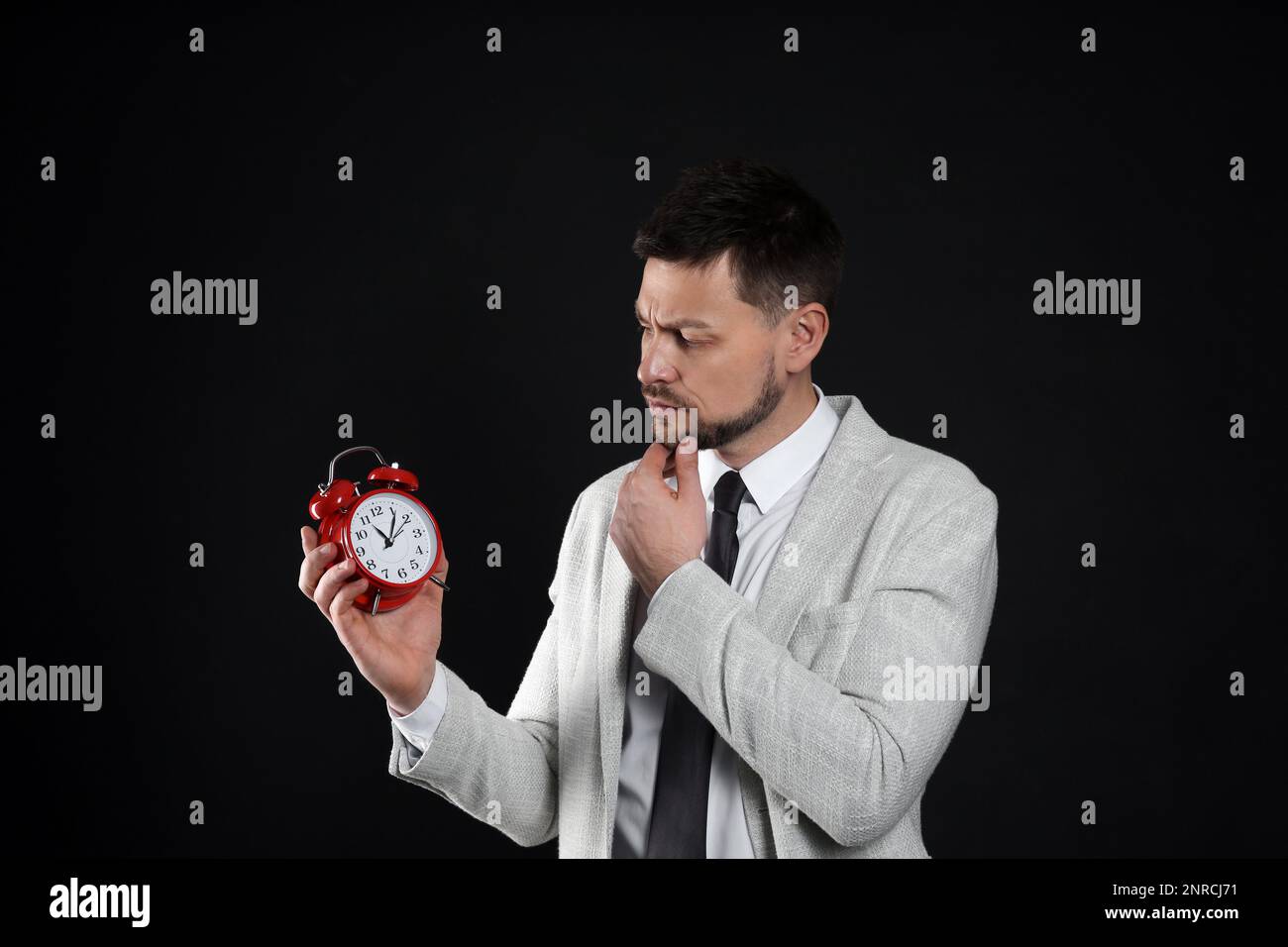 Businessman holding alarm clock on black background. Time management ...