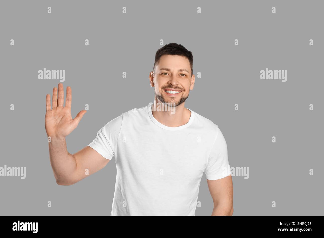 Cheerful man waving to say hello on light grey background Stock Photo ...
