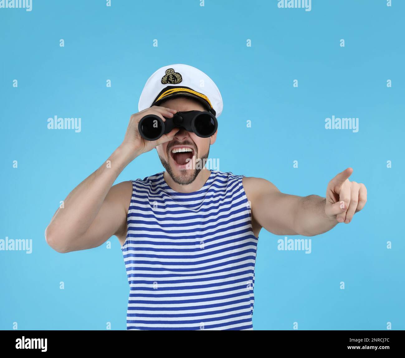 Sailor looking through binoculars and pointing on light blue background ...