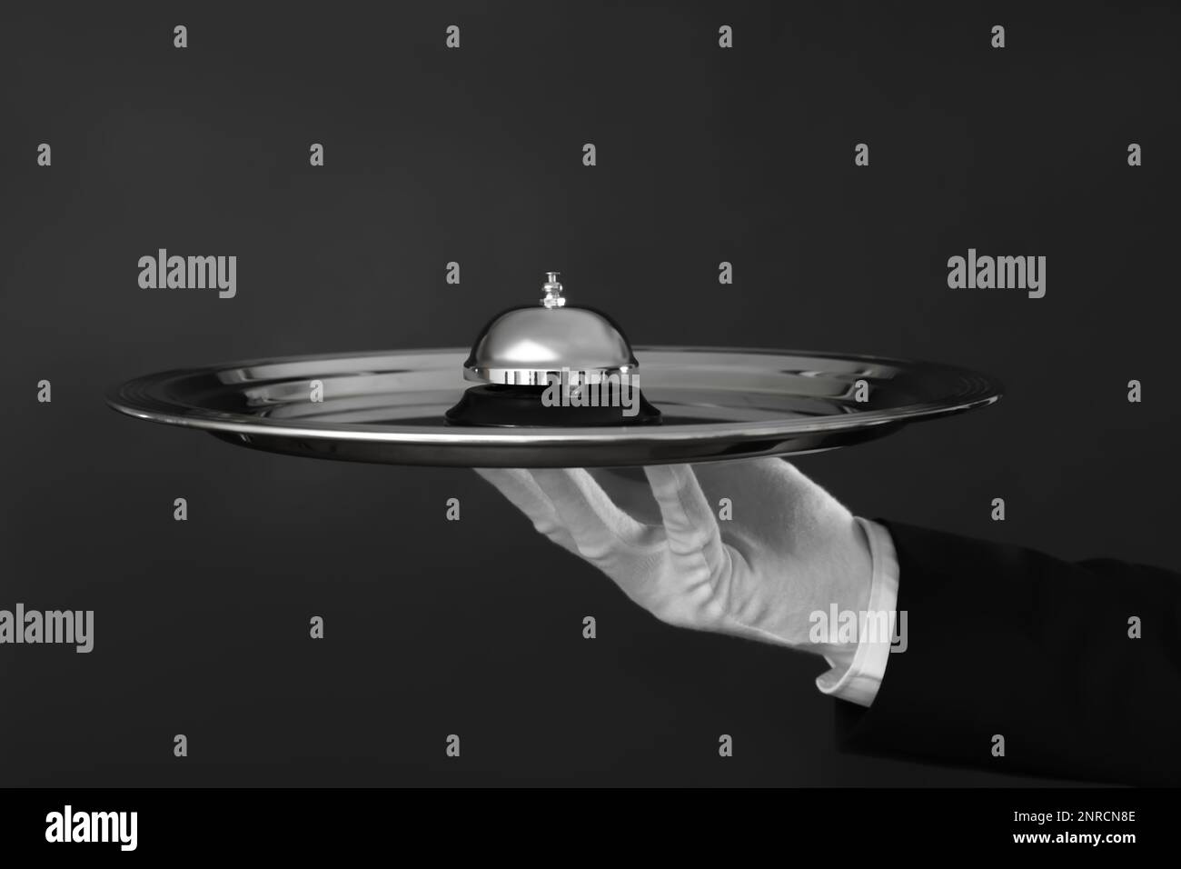 Butler holding metal tray with service bell on black background ...