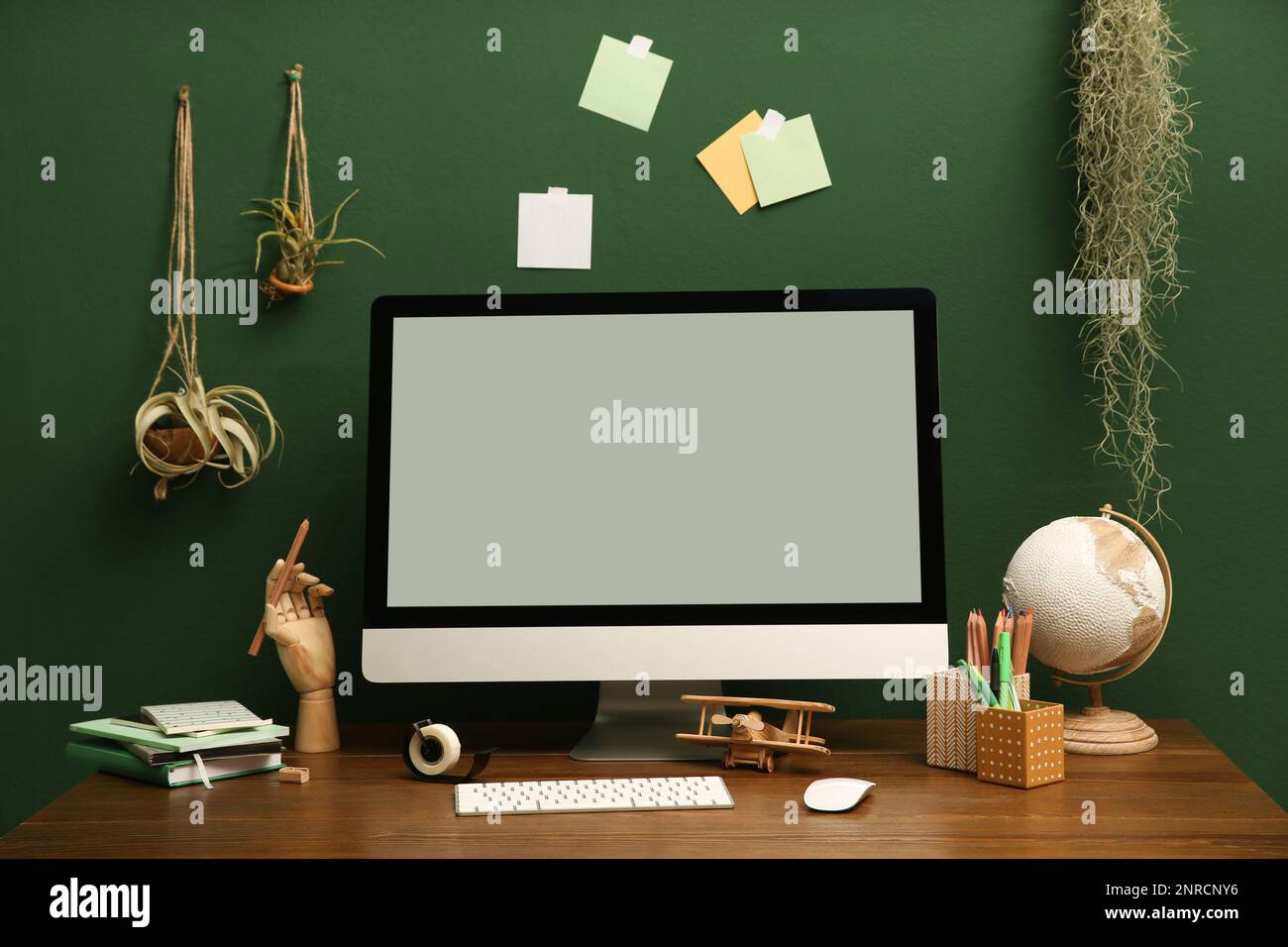 Stylish workplace with blank computer monitor on wooden desk near green ...