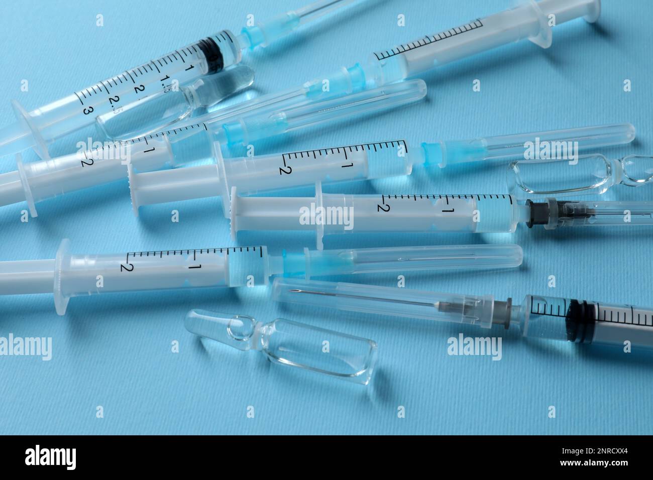 Disposable syringes with needles and ampules on light blue background ...