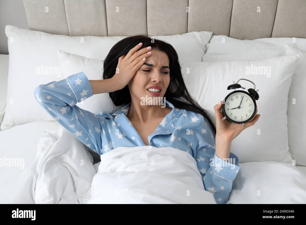 Emotional overslept woman with alarm clock in bed. Being late concept ...