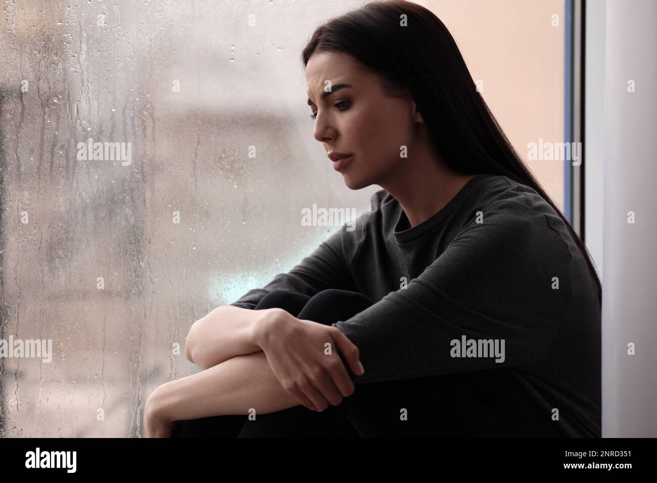 Depressed woman near window on rainy day, space for text Stock Photo ...
