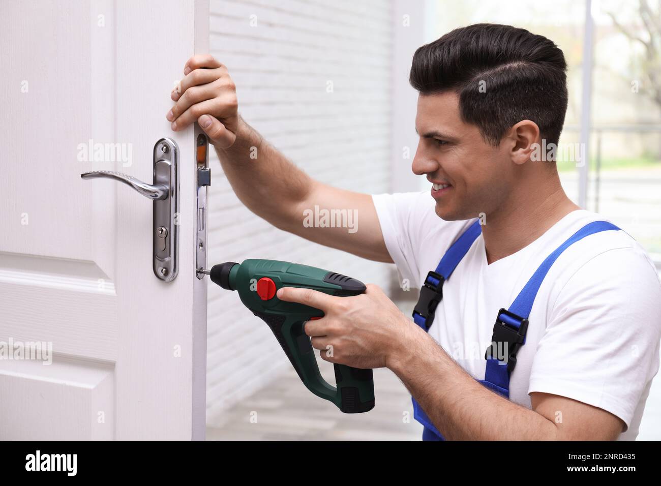 Handyman with screw gun repairing door lock indoors Stock Photo - Alamy