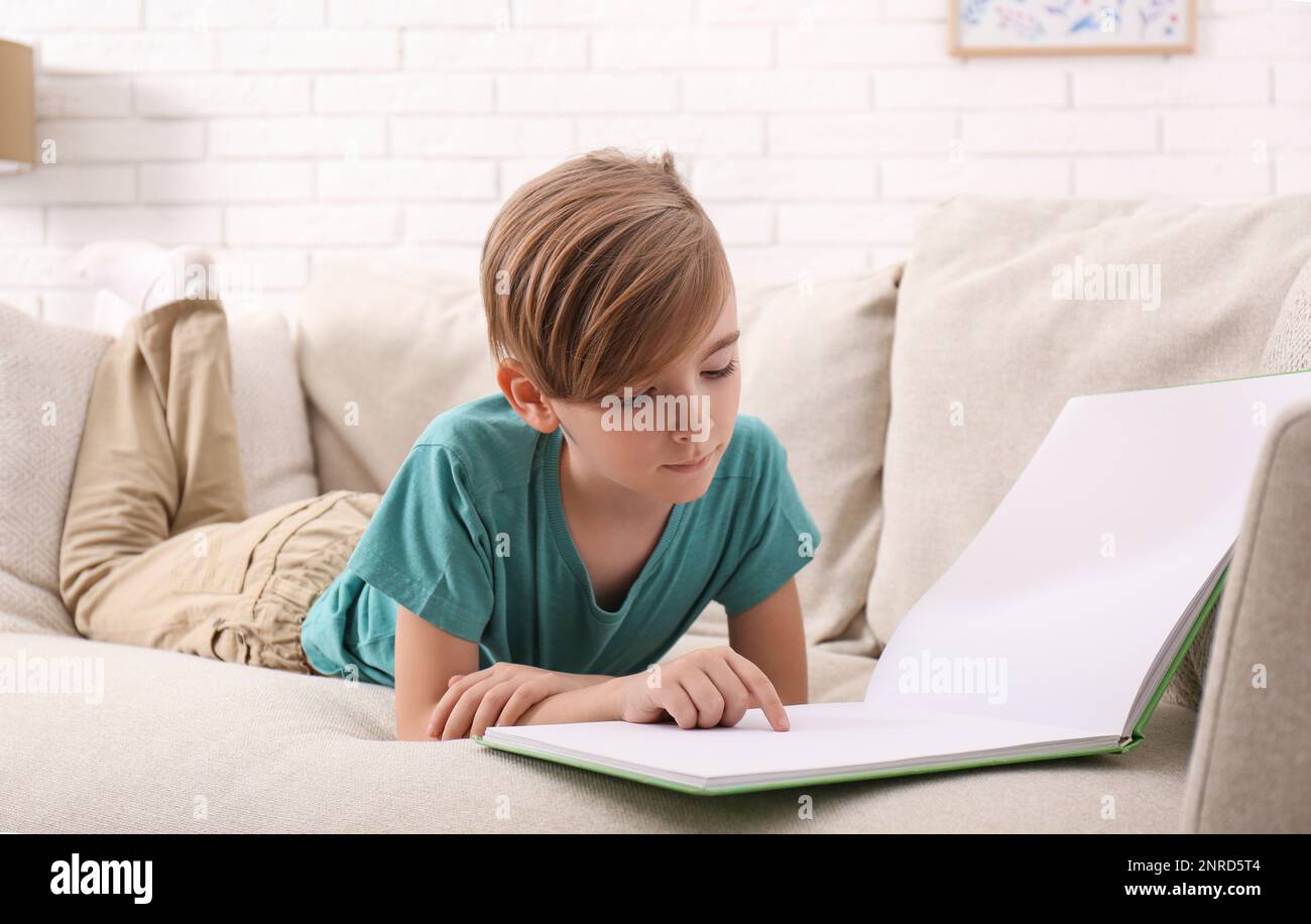 Little boy reading book on sofa at home Stock Photo - Alamy