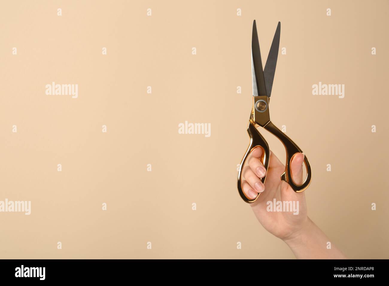 Woman holding sewing scissors on beige background, closeup. Space for ...