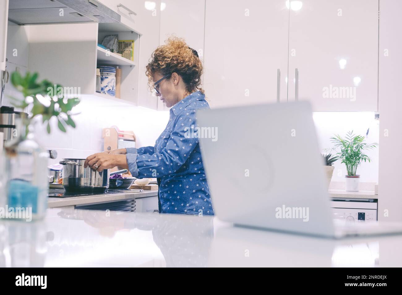 One woman cooking alone at home using pots and laptop computer to watch ...