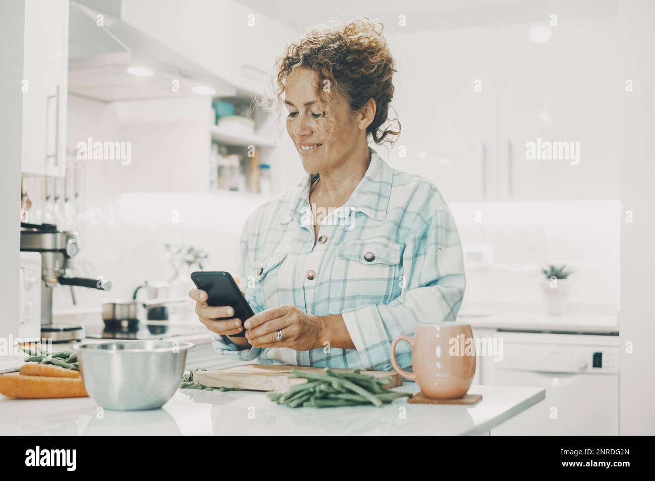Happy woman at home preparing food lunch and watching mobile phone to ...