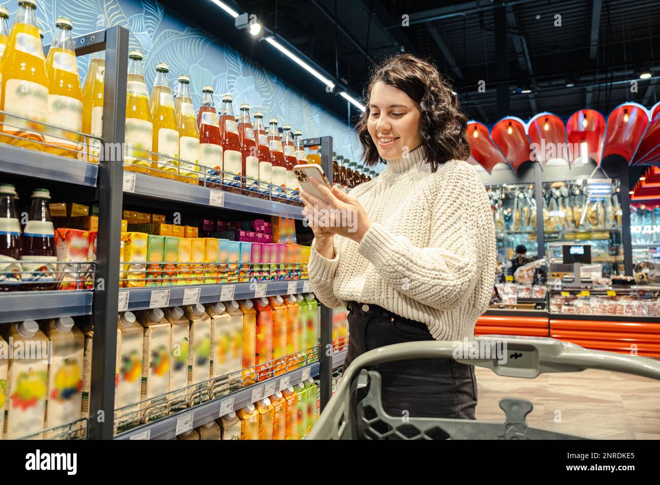 Woman shops juice using phone grocery list in grocery store Stock Photo ...