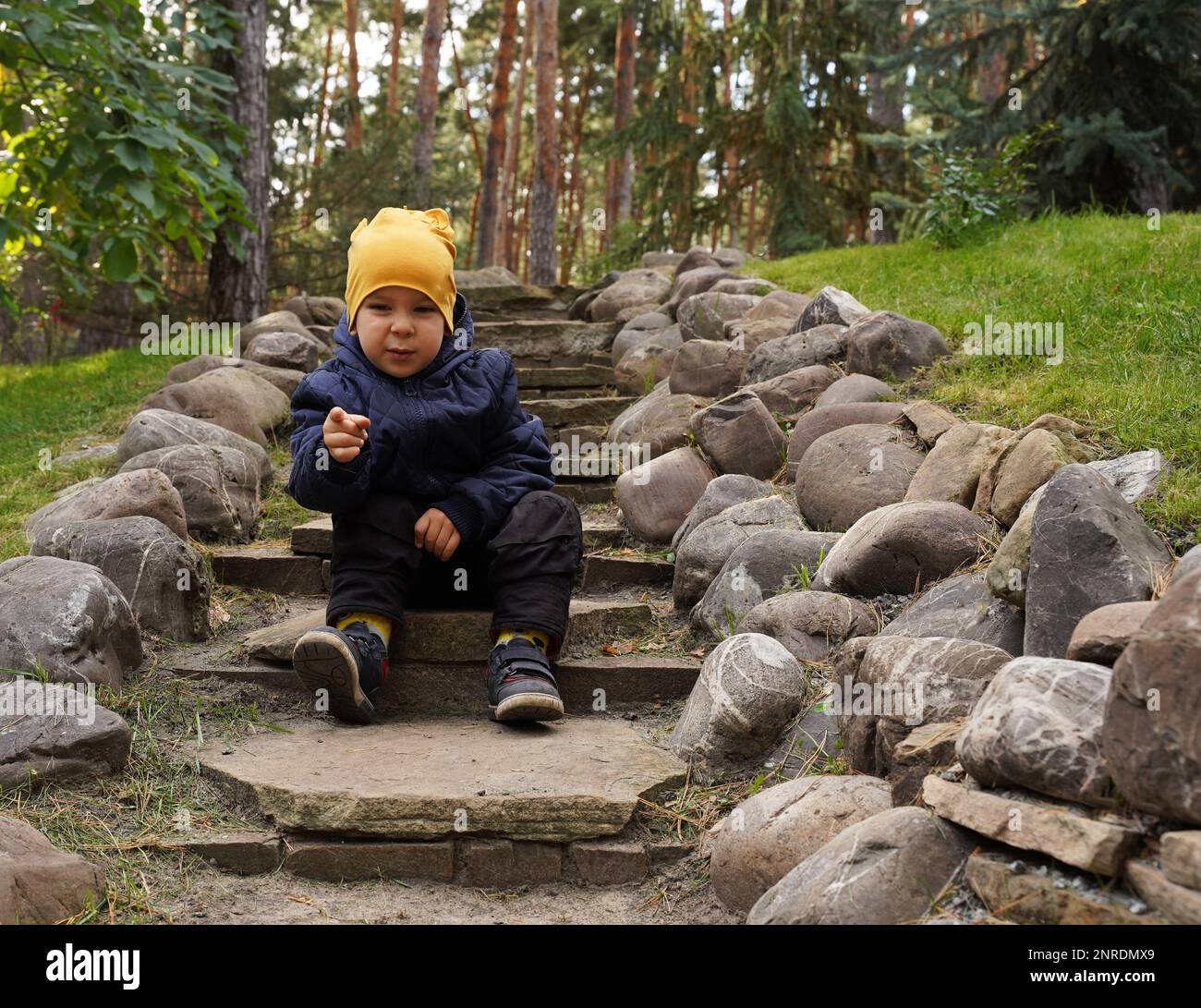 Boy child points his finger at the camera sitting on natural stone ...