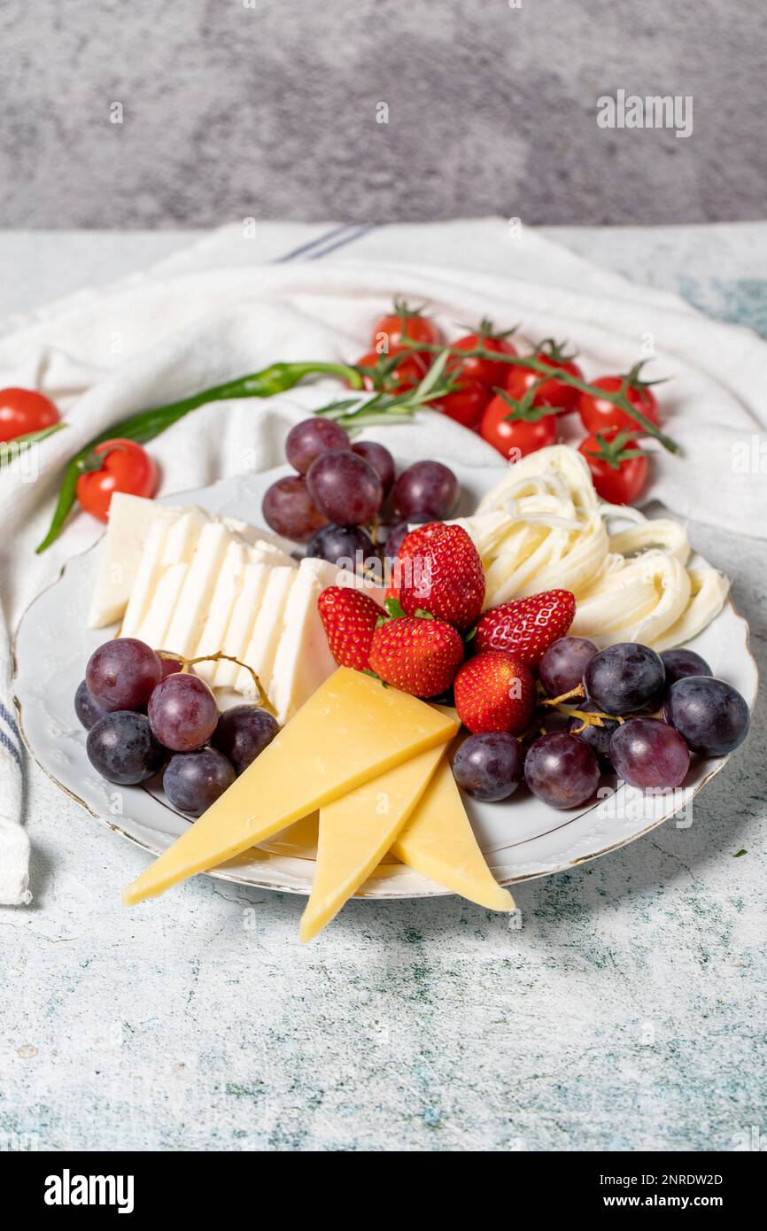 Cold cheese plate, cheese set platter. Strawberry, grape and cheese assortment on gray ...