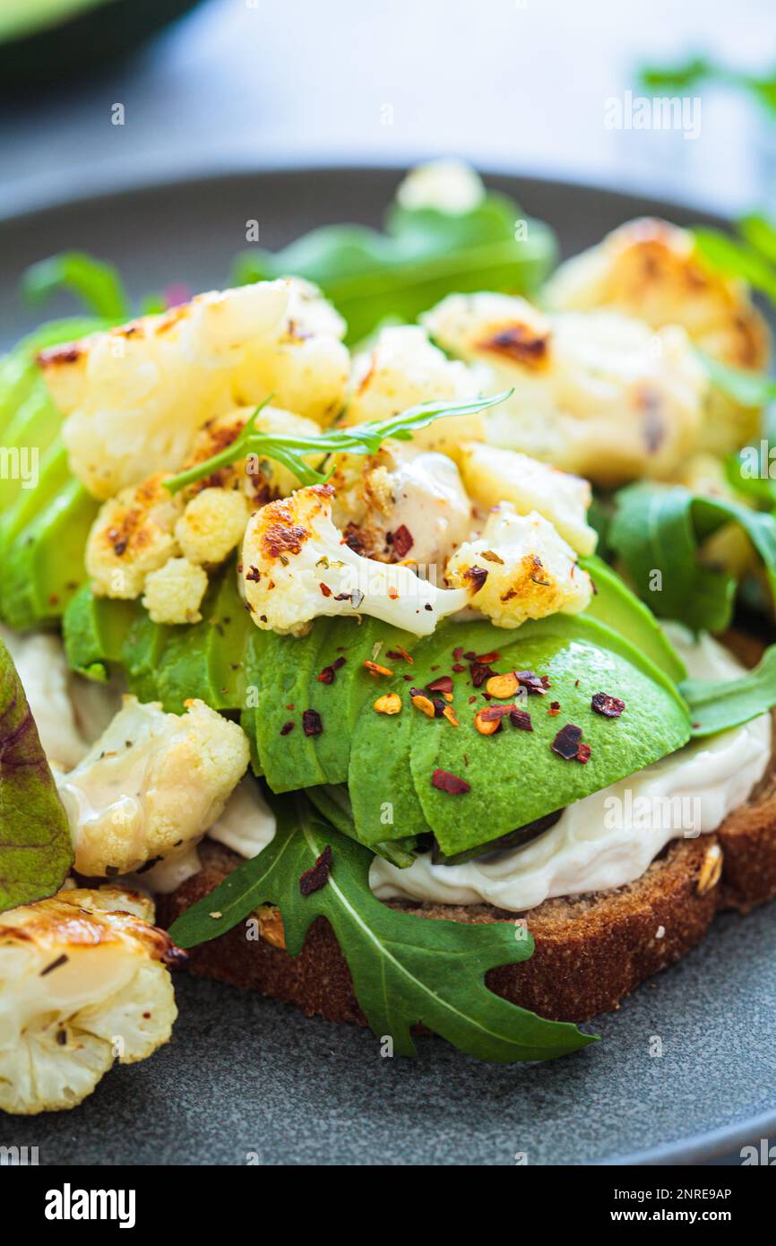 Vegan toast with avocado, baked cauliflower, lettuce and tahini on dark ...