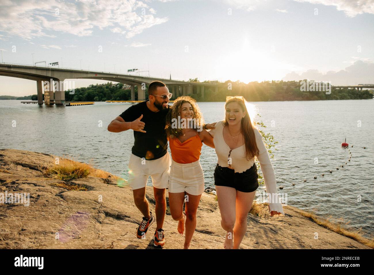 Happy man showing shaka sign while walking with female friends on rock ...