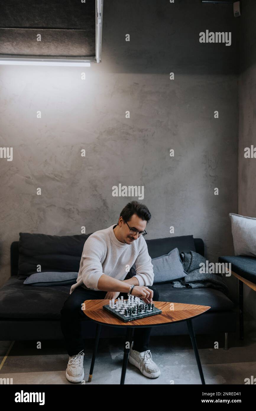 Young male entrepreneur playing chess while sitting on sofa at ...
