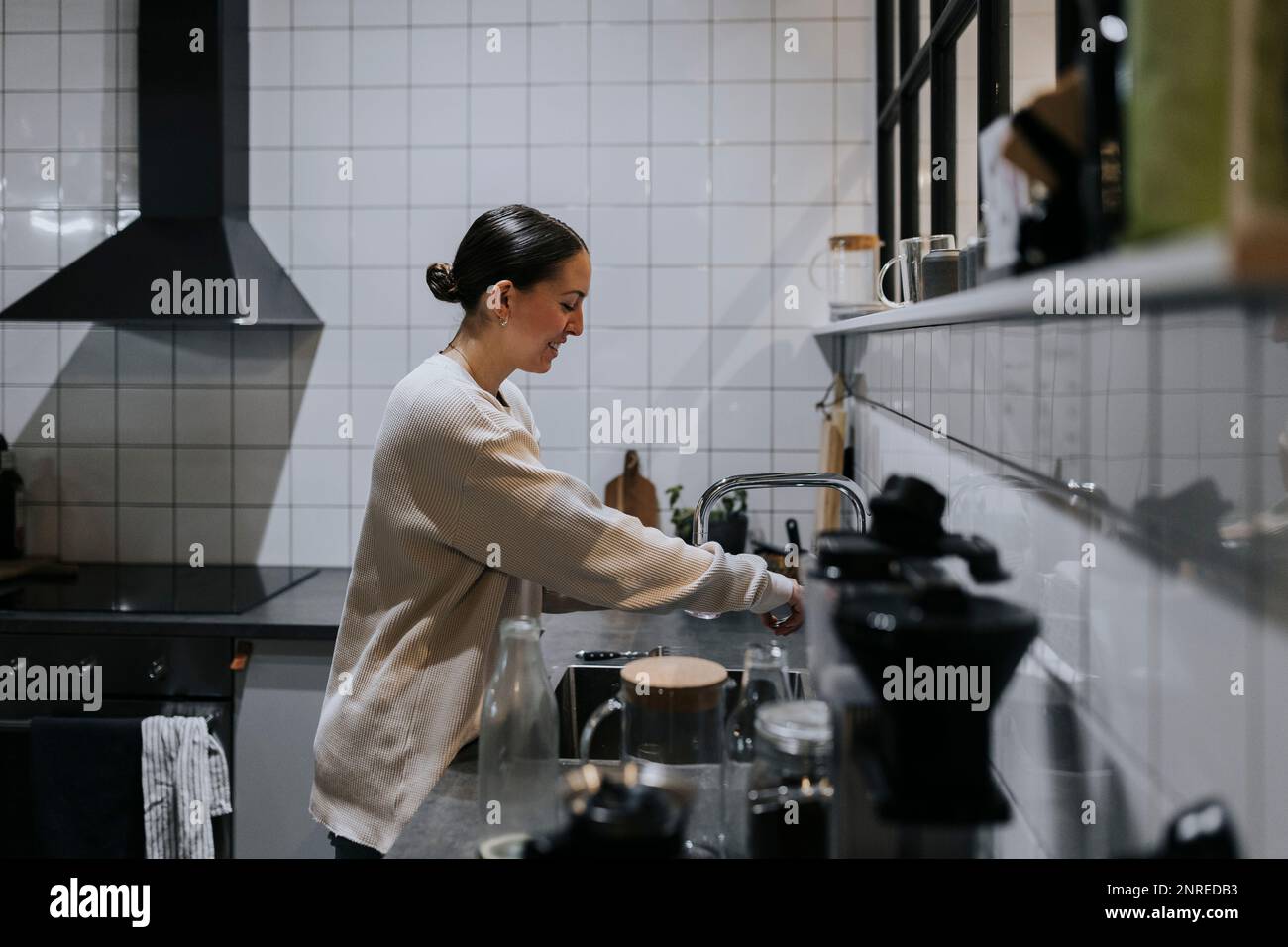 Side view of smiling businesswoman washing glass at sink in office ...