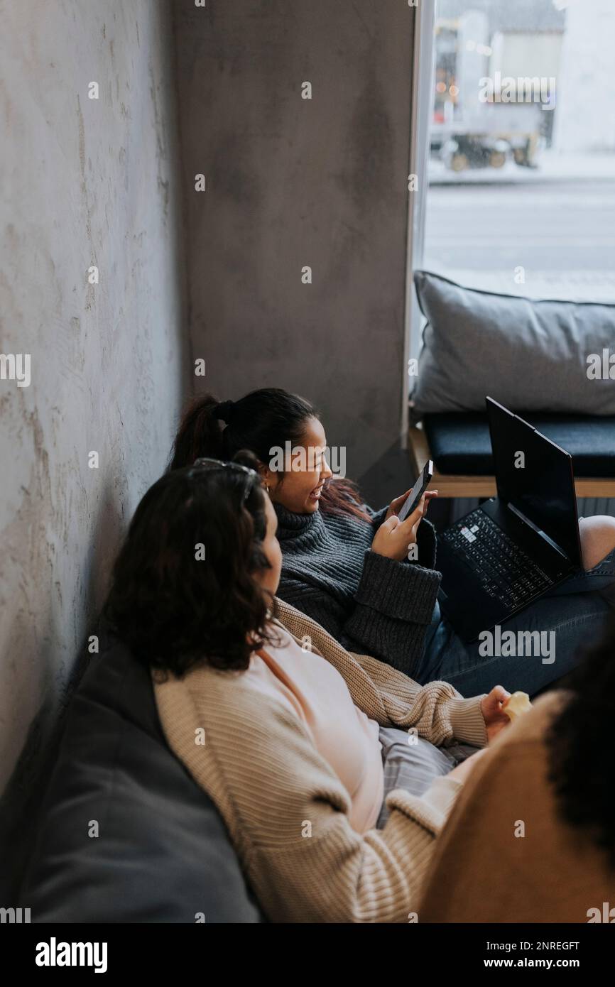 Happy businesswoman using smart phone by female colleague during break ...