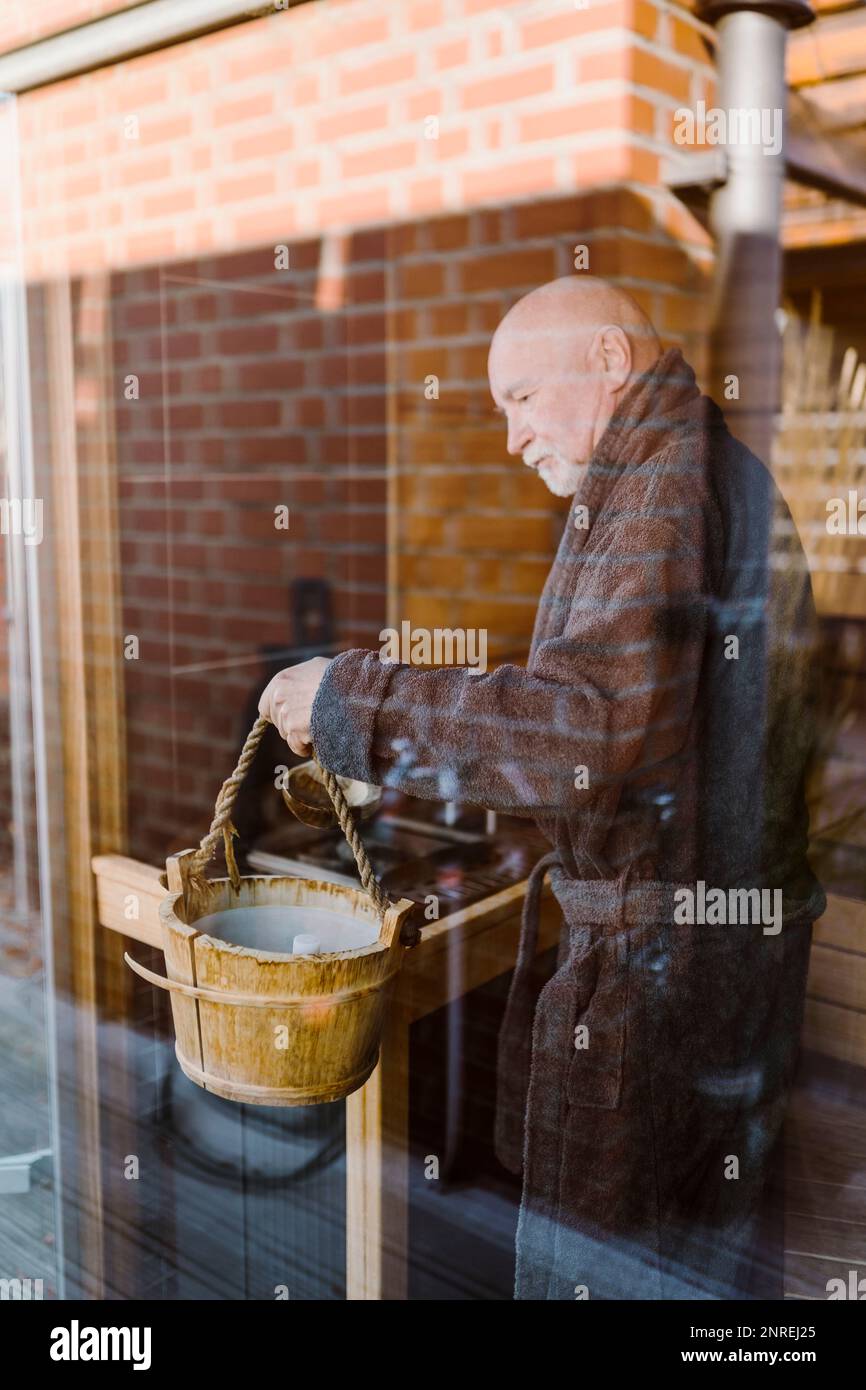 Side view of senior man holding bucket while standing in sauna seen ...
