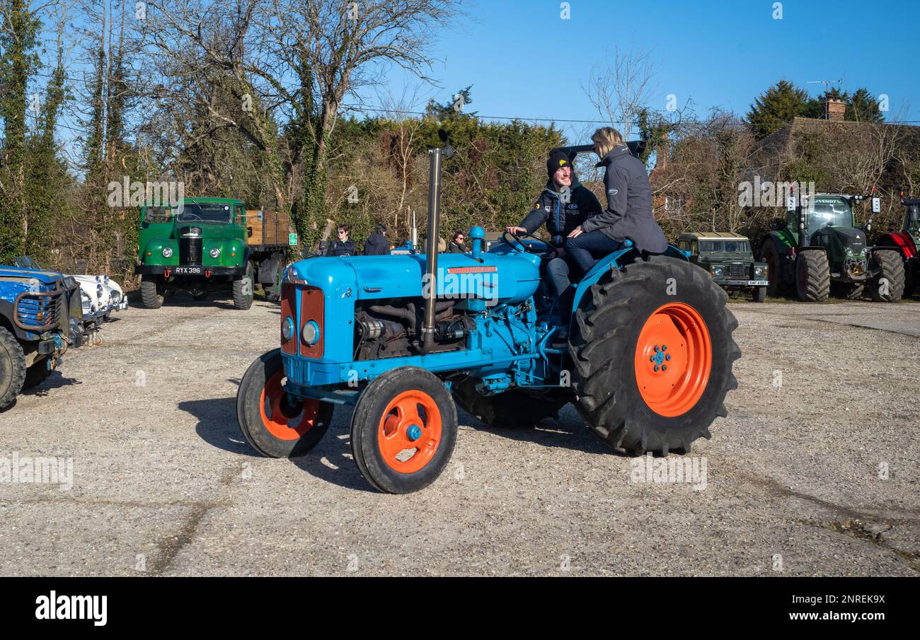 A man driving a vintage Fordson tractor looks at his partner sitting on ...