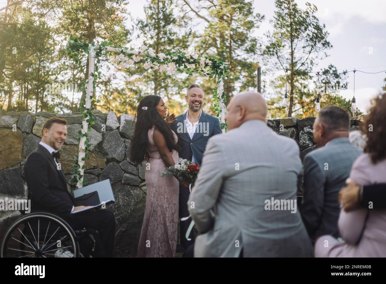 Happy newlywed couple holding bouquet by guests and minister with ...