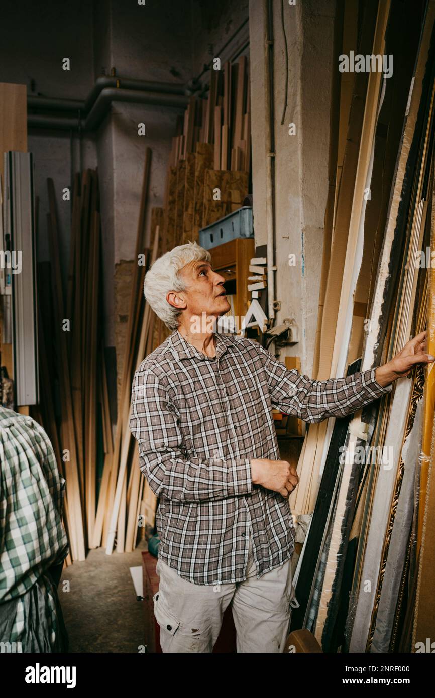 Male senior entrepreneur selecting wood while standing at workshop ...